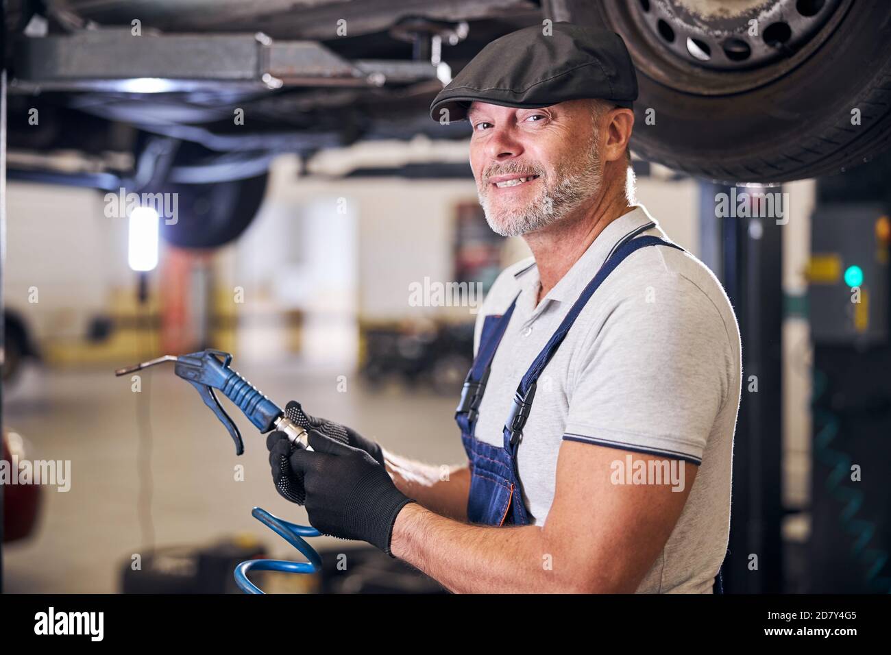 Cheerful auto mechanic using air blow gun at service garage Stock Photo ...