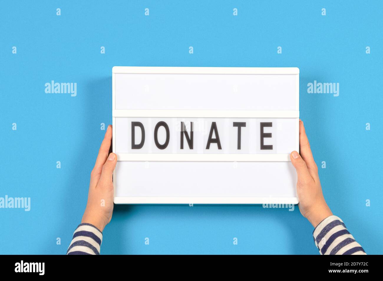 Hands holding light box with Donate word text over light blue ...