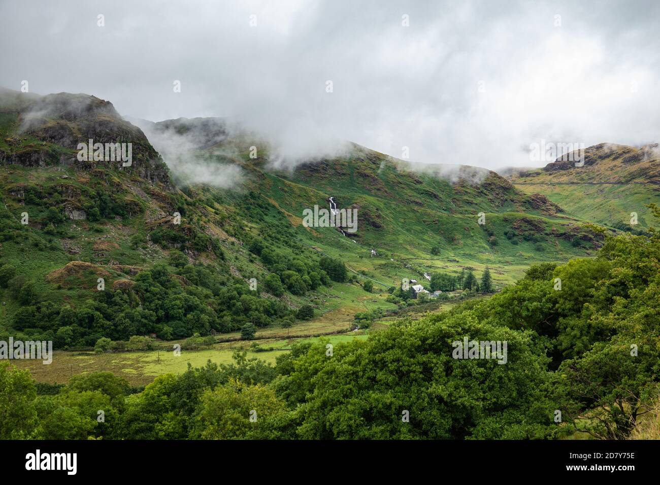 A waterfall on a hillside stream descends into a cloud covered valley ...