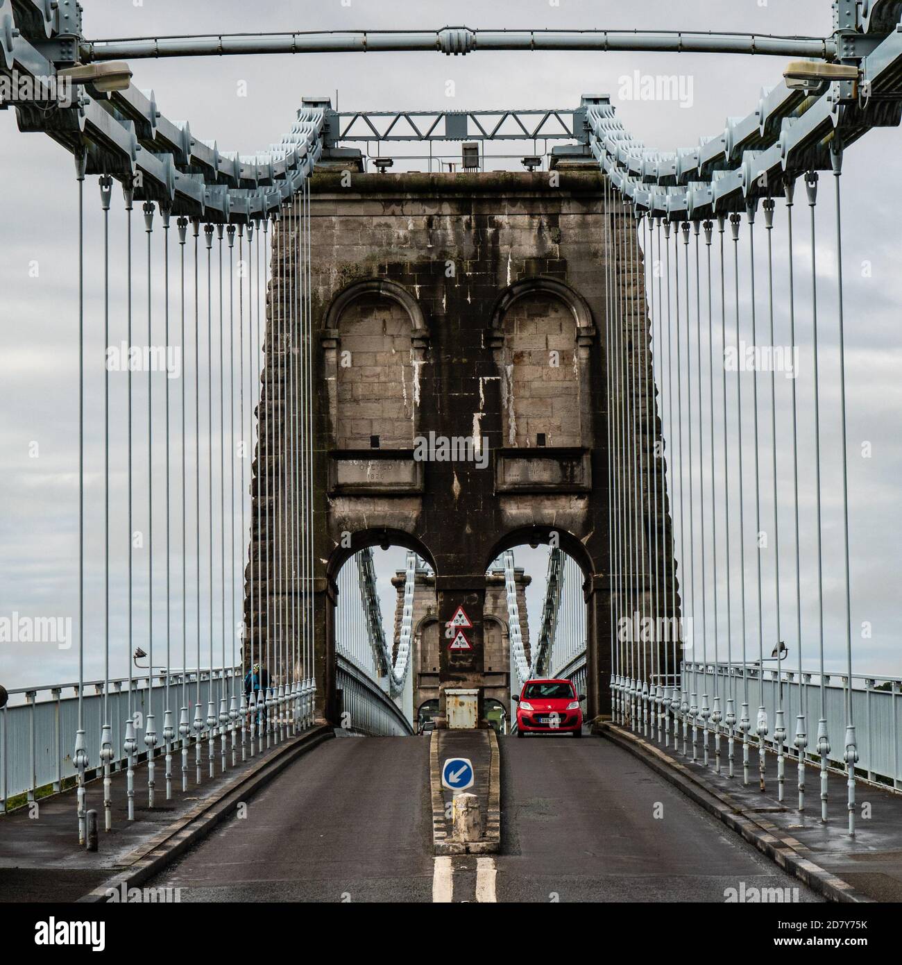 A red car passes under the arches of the historic Menai Suspension ...