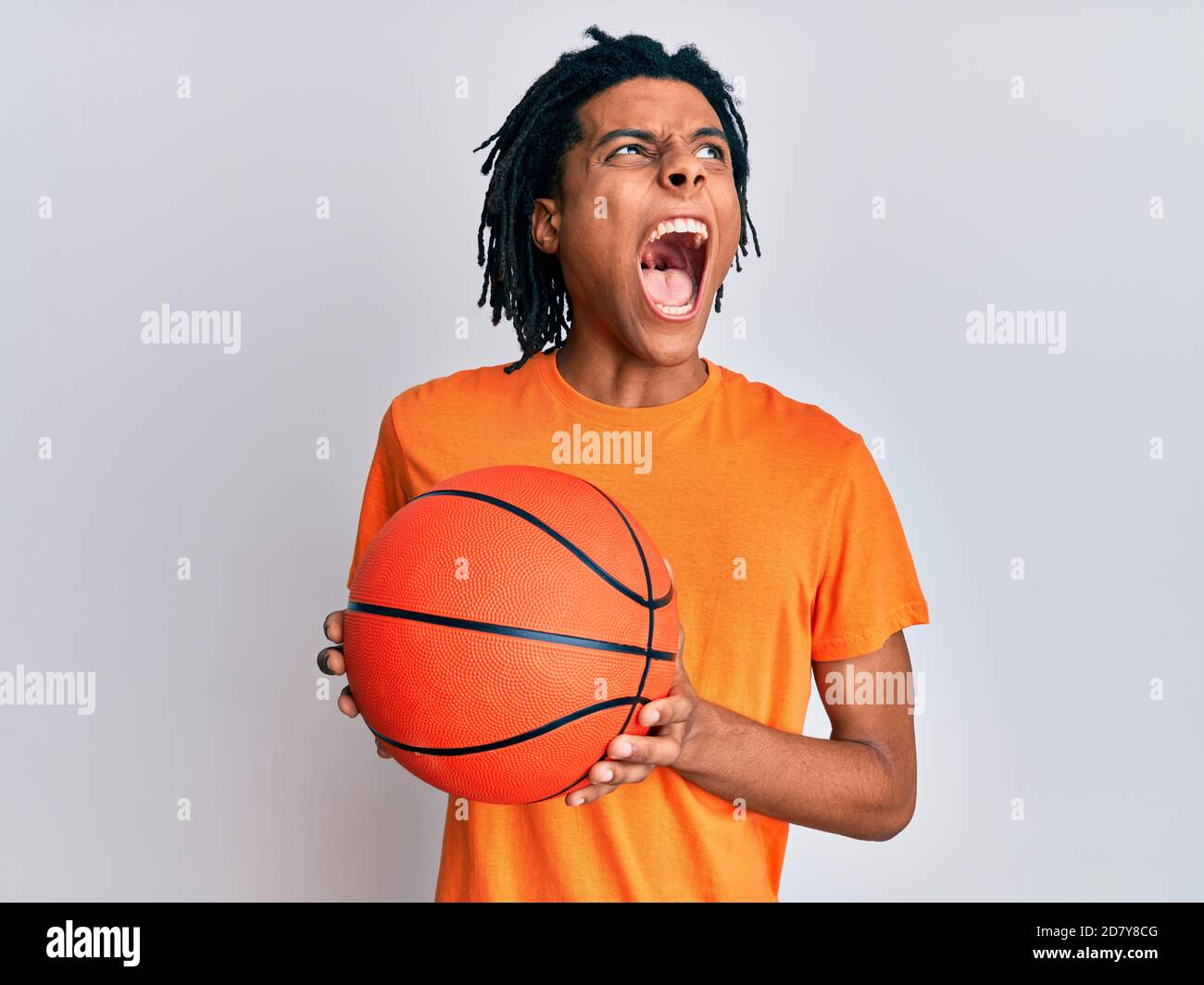 Young african american man holding basketball ball angry and mad ...