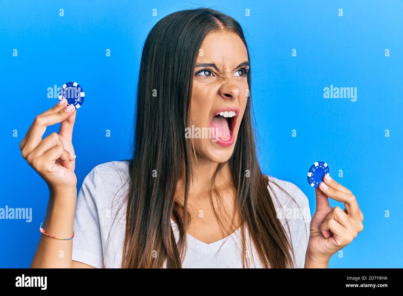 Young hispanic woman holding poker chips angry and mad screaming ...