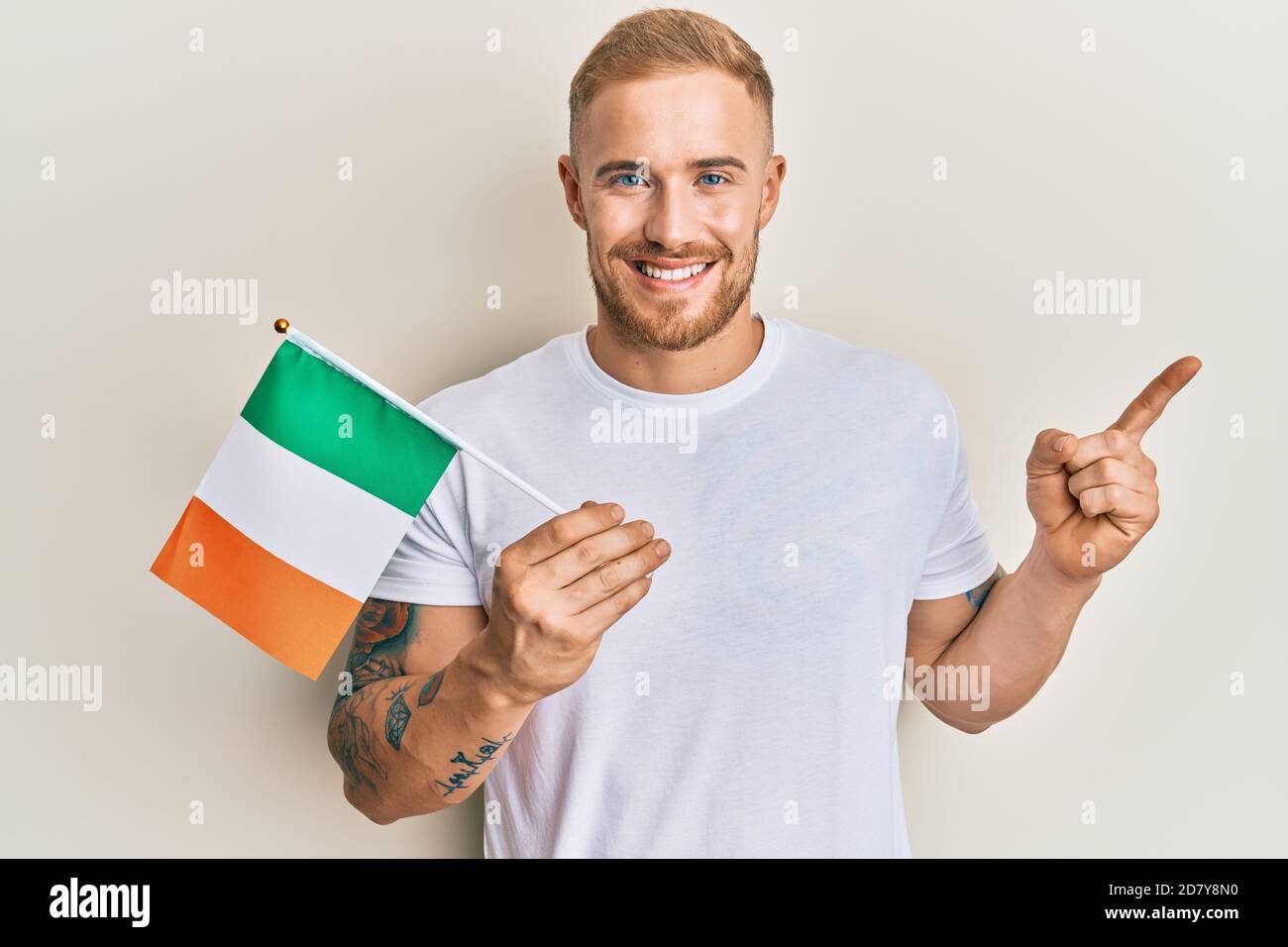 Young caucasian man holding irish flag smiling happy pointing with hand ...