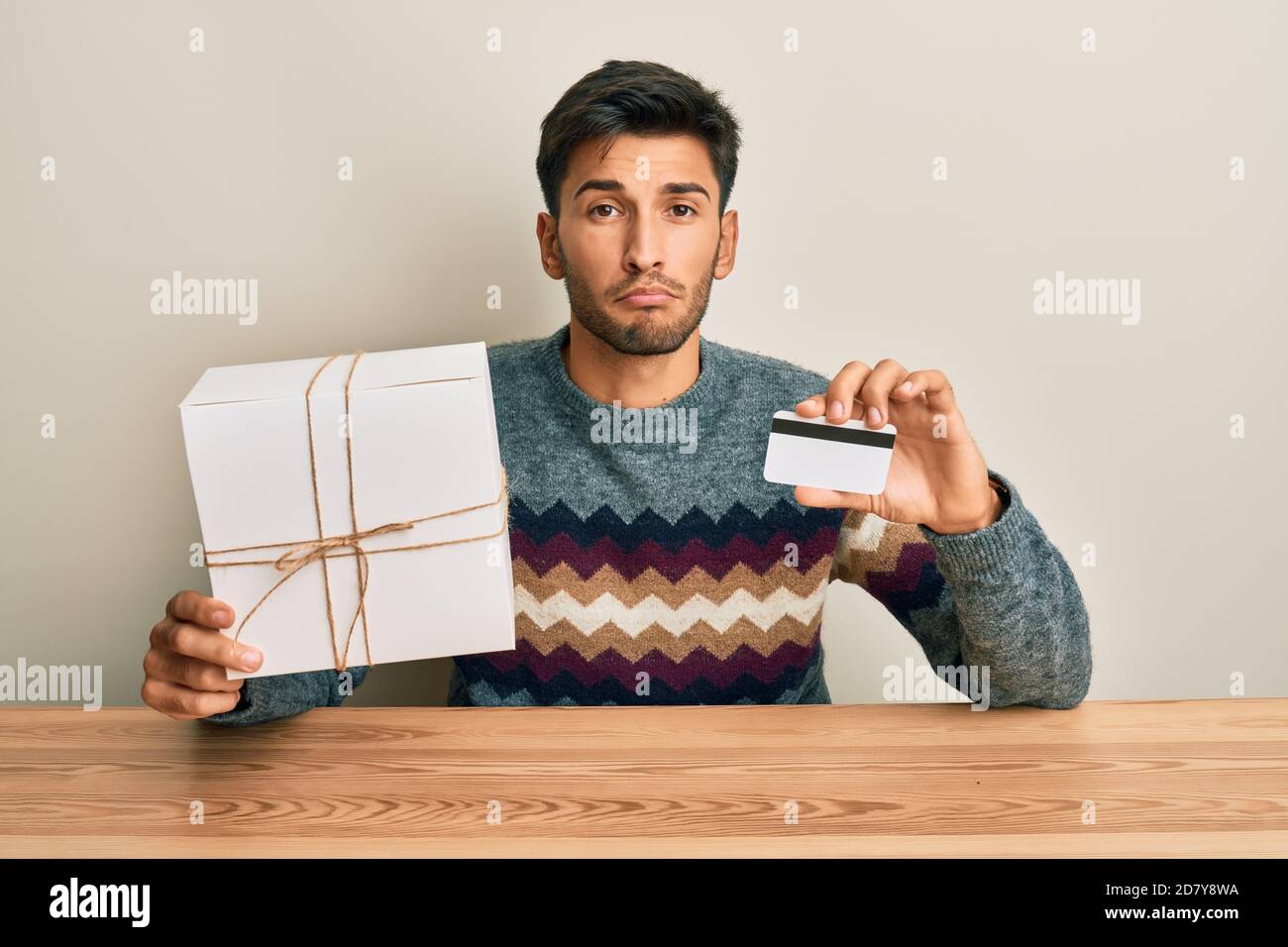Young handsome man holding gift and credit card depressed and worry for ...