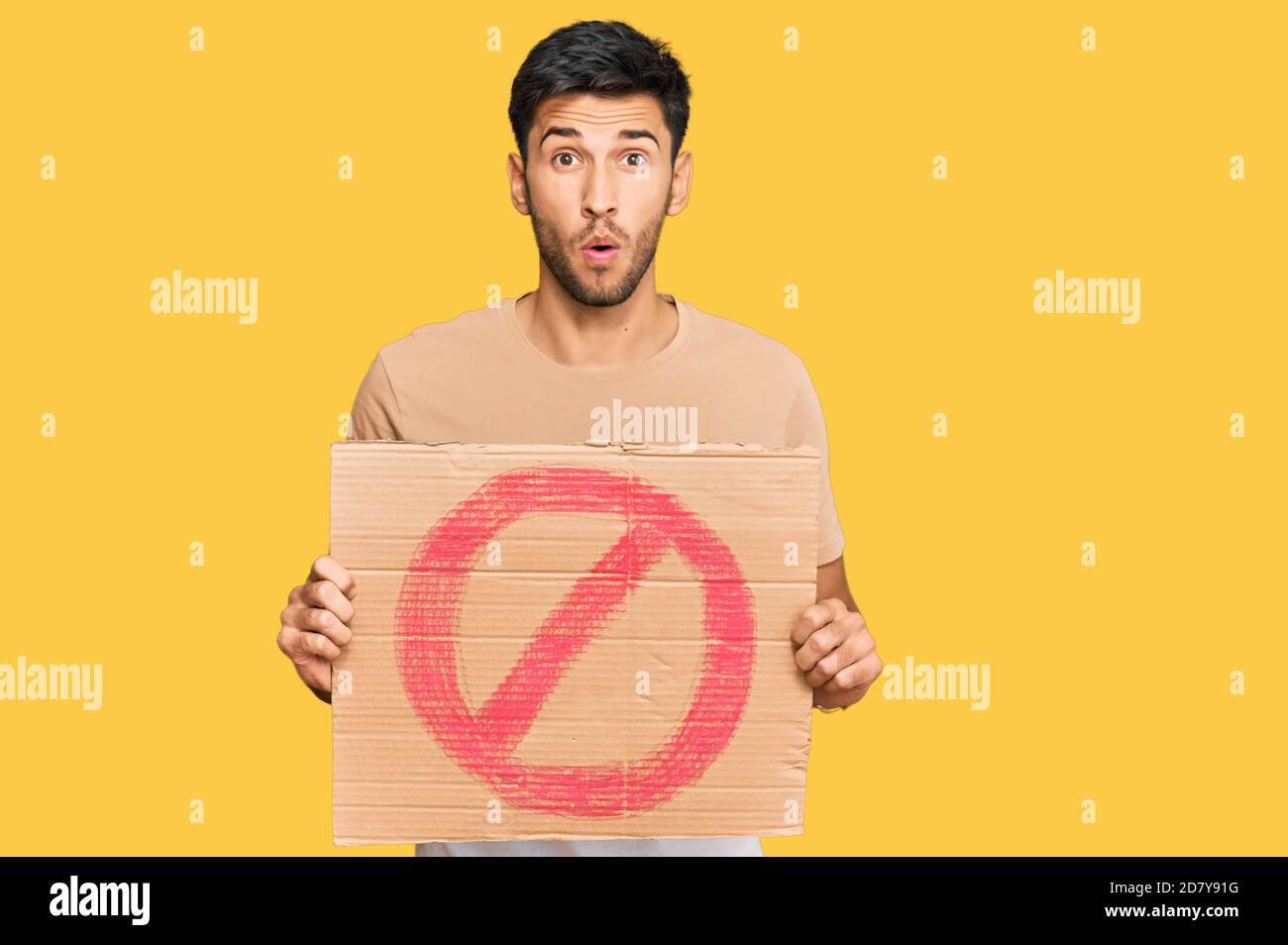 Young handsome man holding prohibited warning banner scared and amazed ...