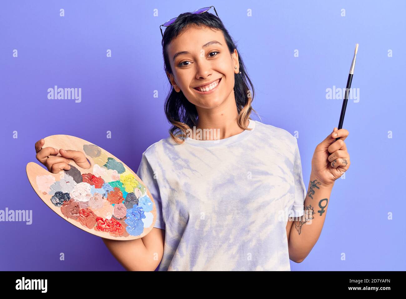 Young woman holding paintbrush and palette looking positive and happy ...