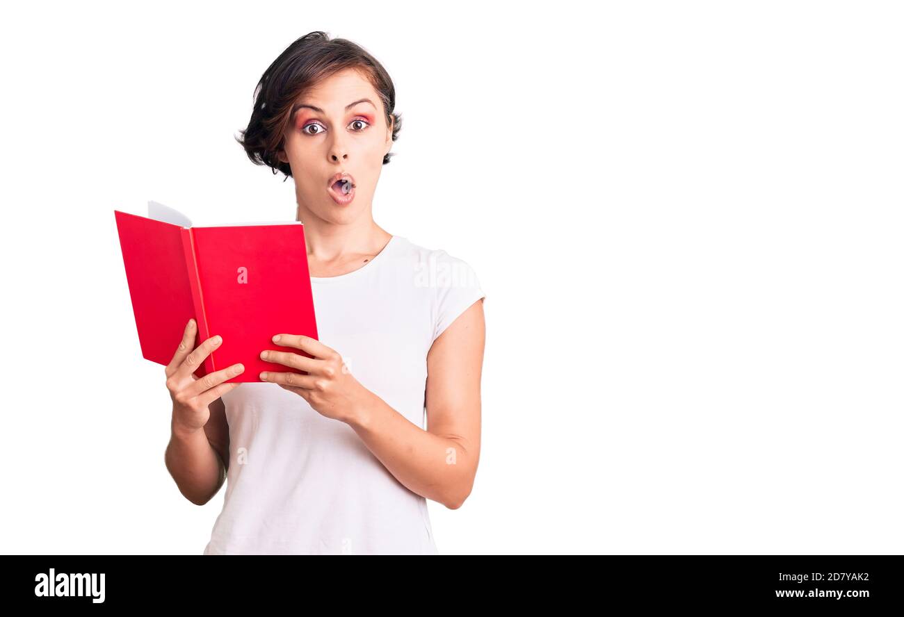 Beautiful young woman with short hair reading a book scared and amazed ...