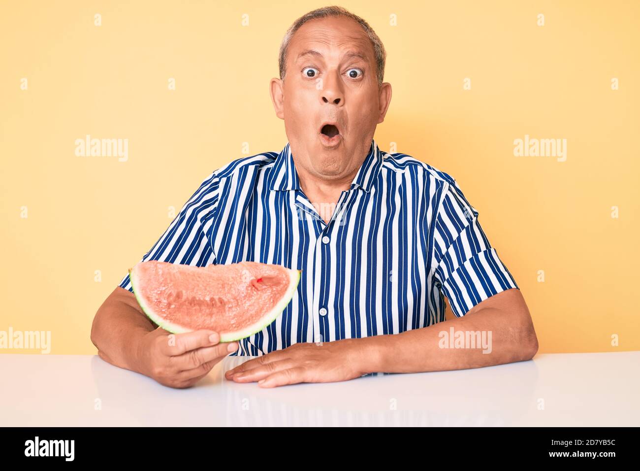 Senior handsome man with gray hair eating sweet watermelon slice scared ...
