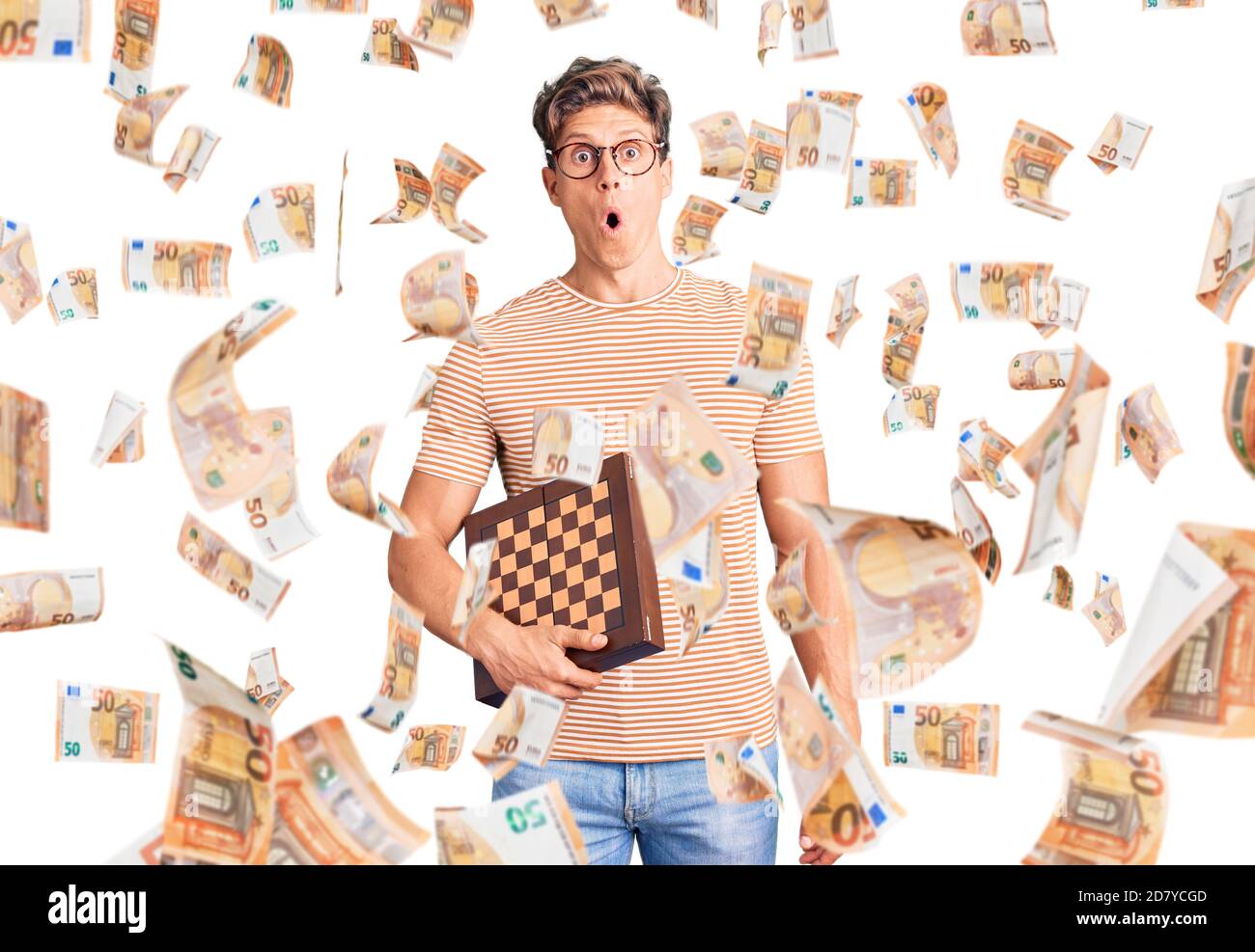Young handsome man holding chess scared and amazed with open mouth for ...
