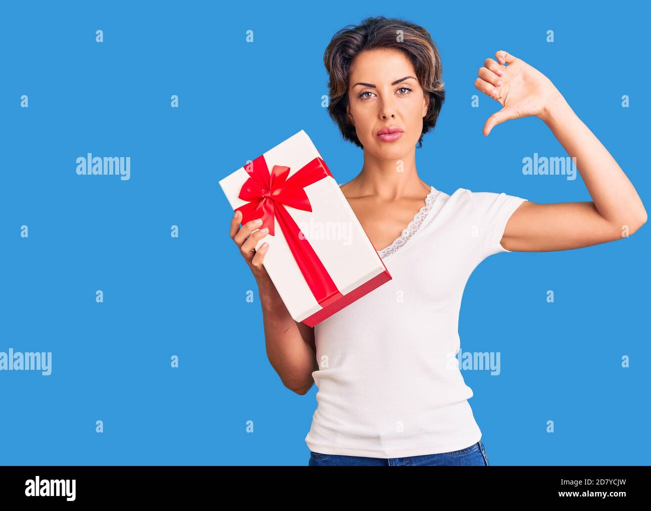 Young beautiful woman holding gift with angry face, negative sign ...