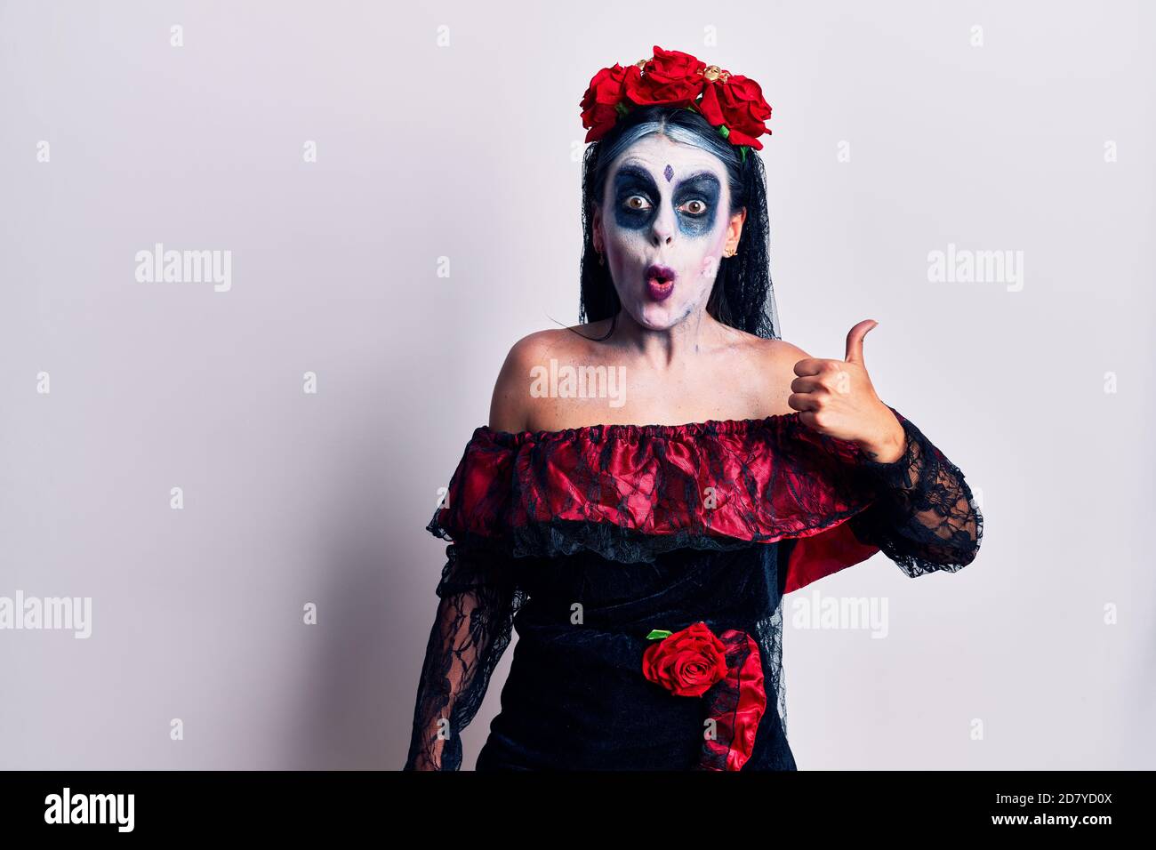 Young woman wearing mexican day of the dead makeup surprised pointing ...