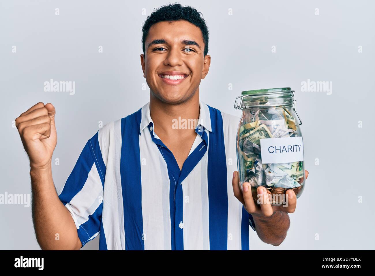 Young arab man holding charity jar with money screaming proud ...