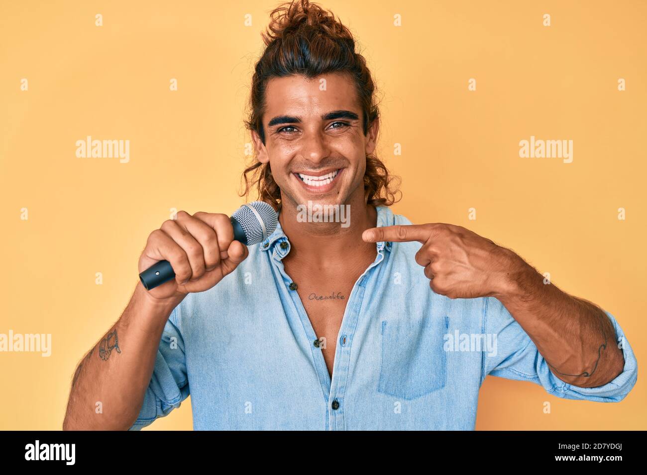 Young hispanic man singing song using microphone smiling happy pointing ...