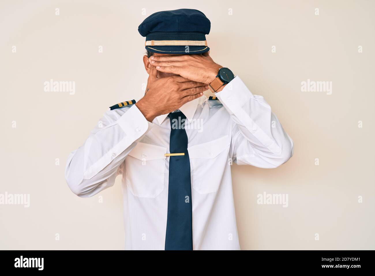 Young hispanic man wearing airplane pilot uniform covering eyes and ...