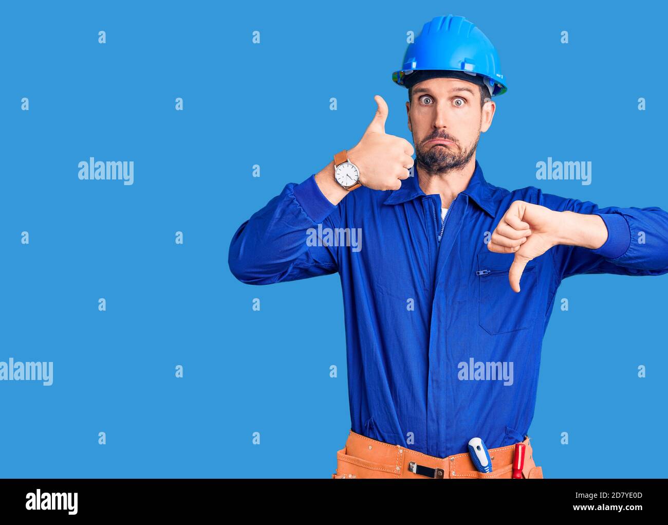 Young handsome man wearing worker uniform and hardhat pointing aside ...