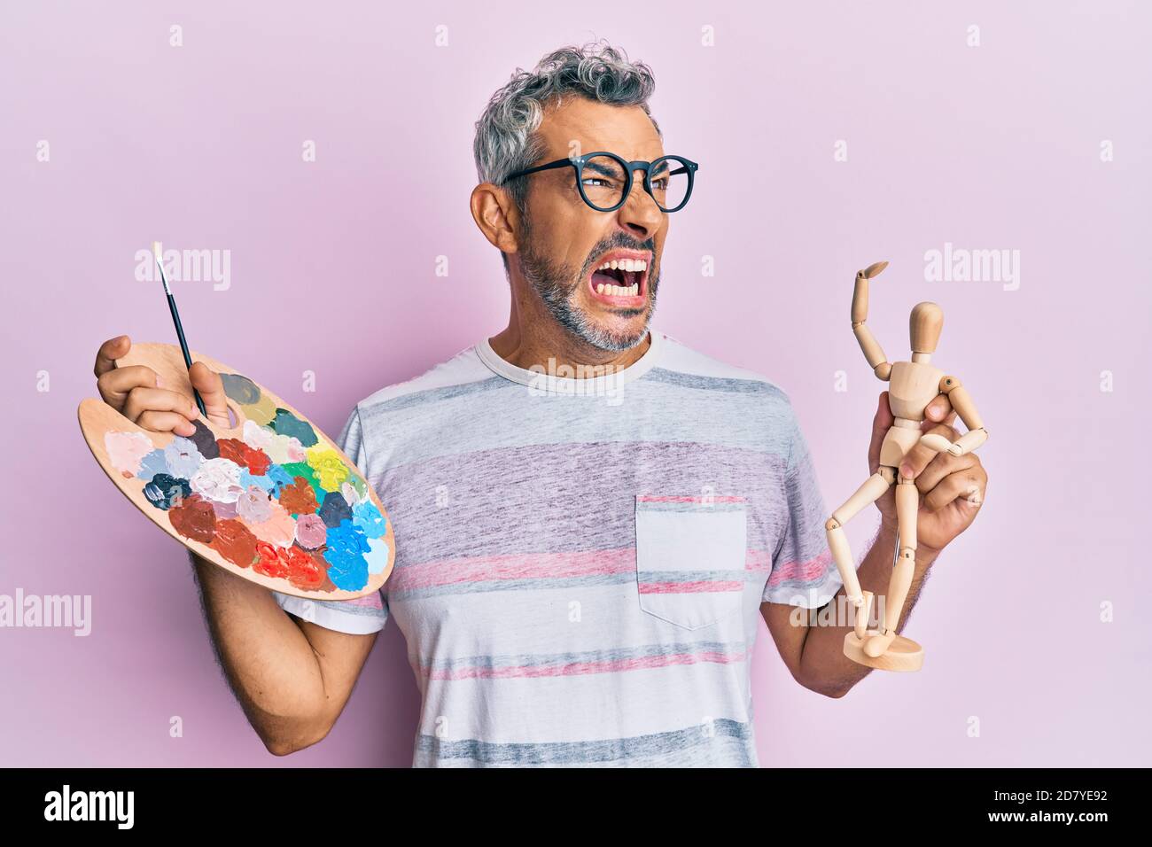 Middle age grey-haired man holding palette and manikin angry and mad ...