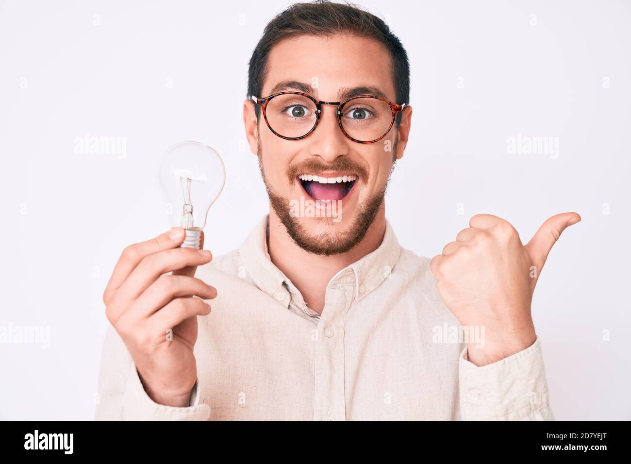 Young handsome man holding lightbulb for inspiration and idea pointing ...