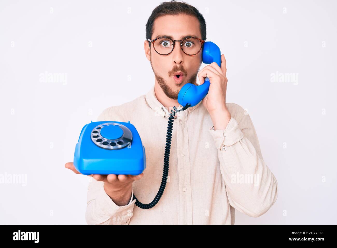 Young handsome man holding vintage telephone scared and amazed with ...