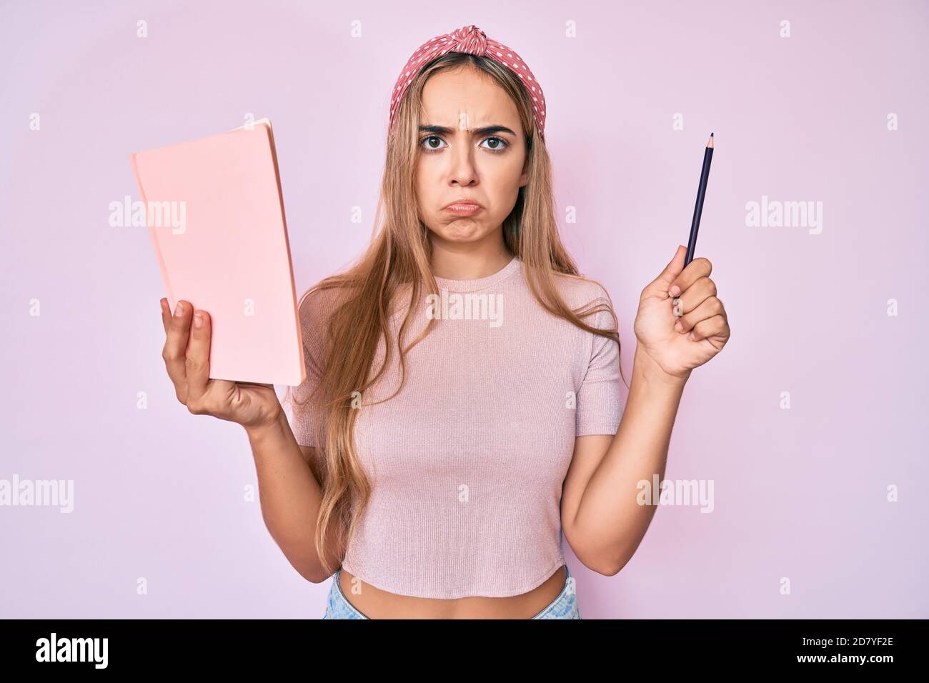 Young beautiful blonde woman holding book and pencil depressed and ...