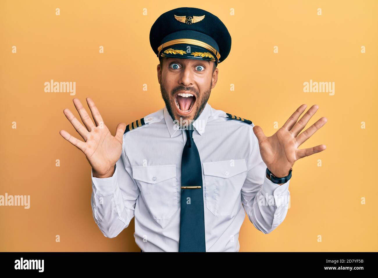 Handsome hispanic man wearing airplane pilot uniform celebrating crazy ...