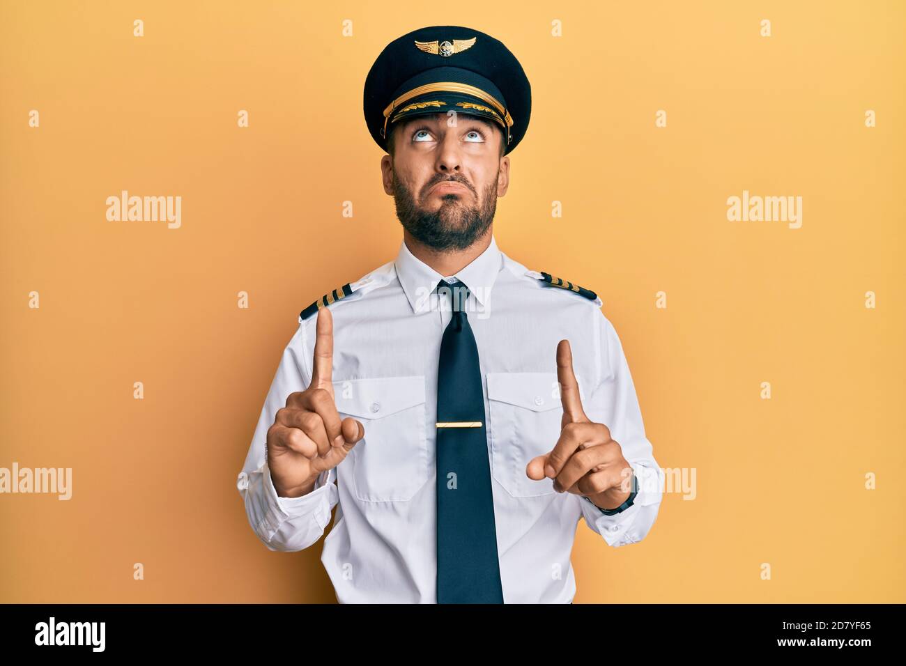 Handsome hispanic man wearing airplane pilot uniform pointing up ...