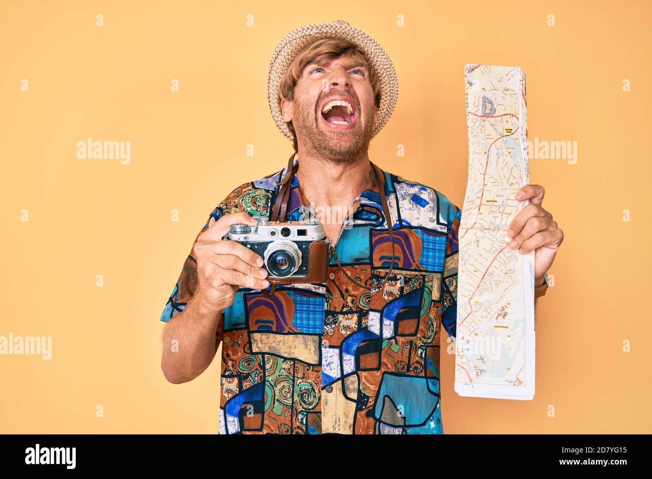 Young blond man holding vintage camera and city map angry and mad ...