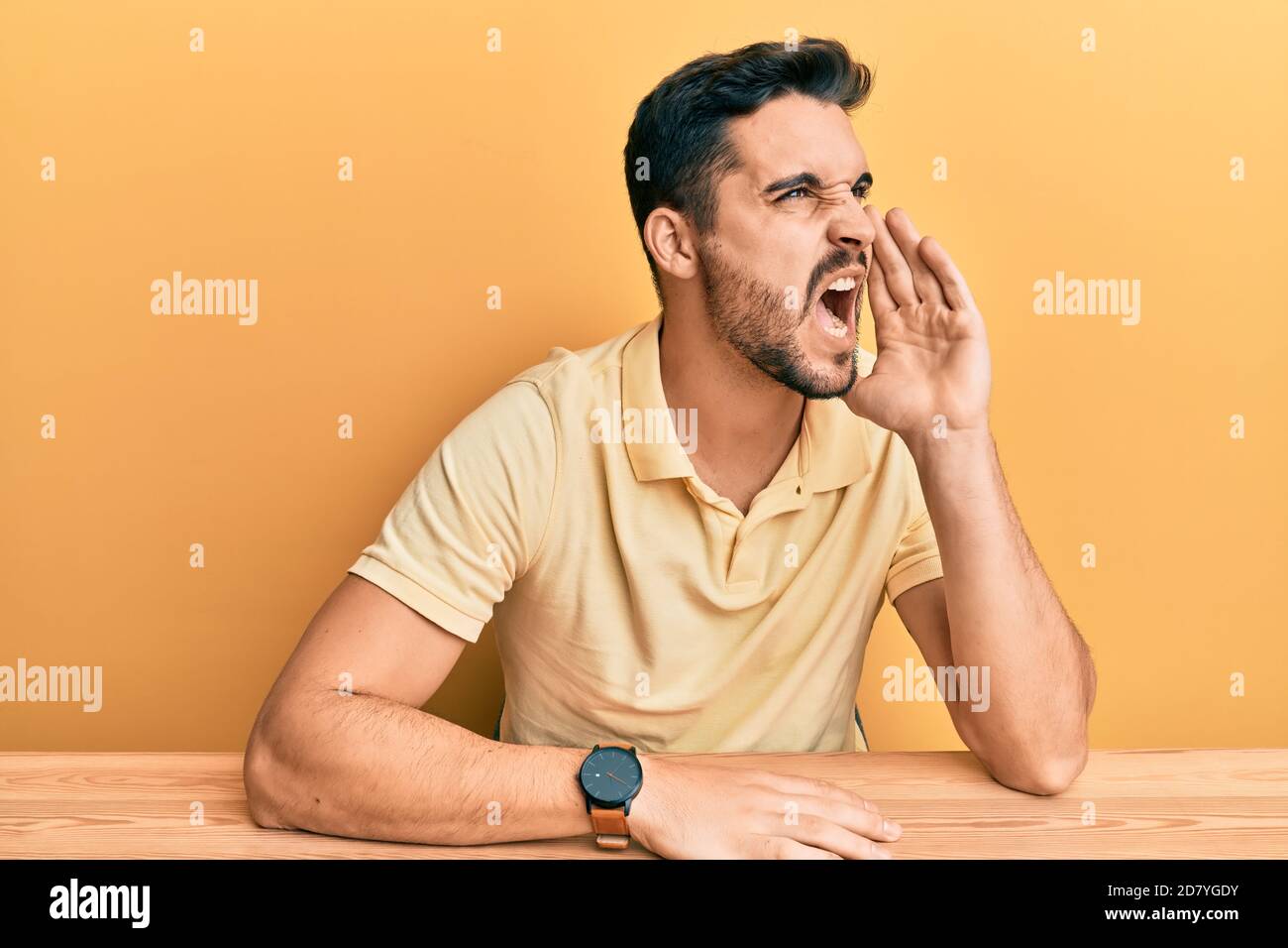 Young hispanic man wearing casual clothes sitting on the table shouting ...