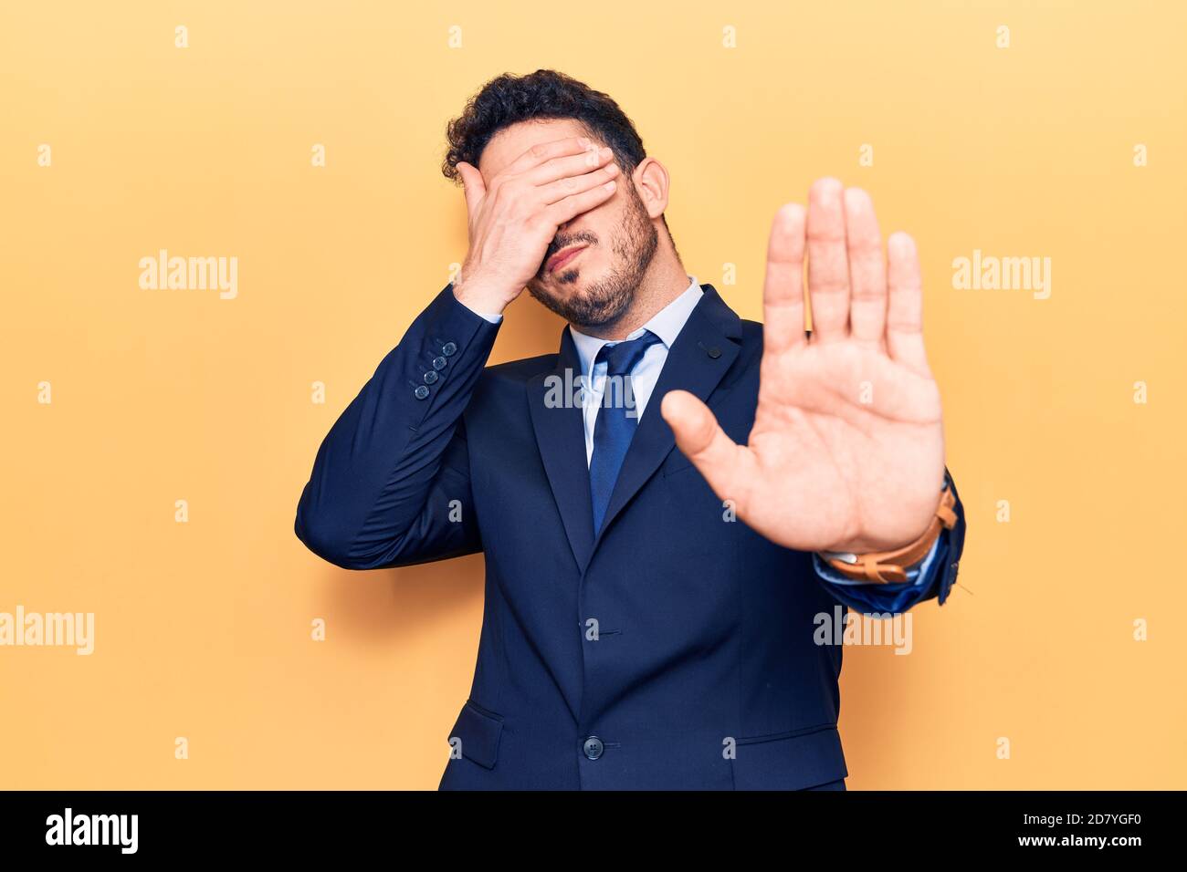 Young hispanic man wearing suit covering eyes with hands and doing stop ...