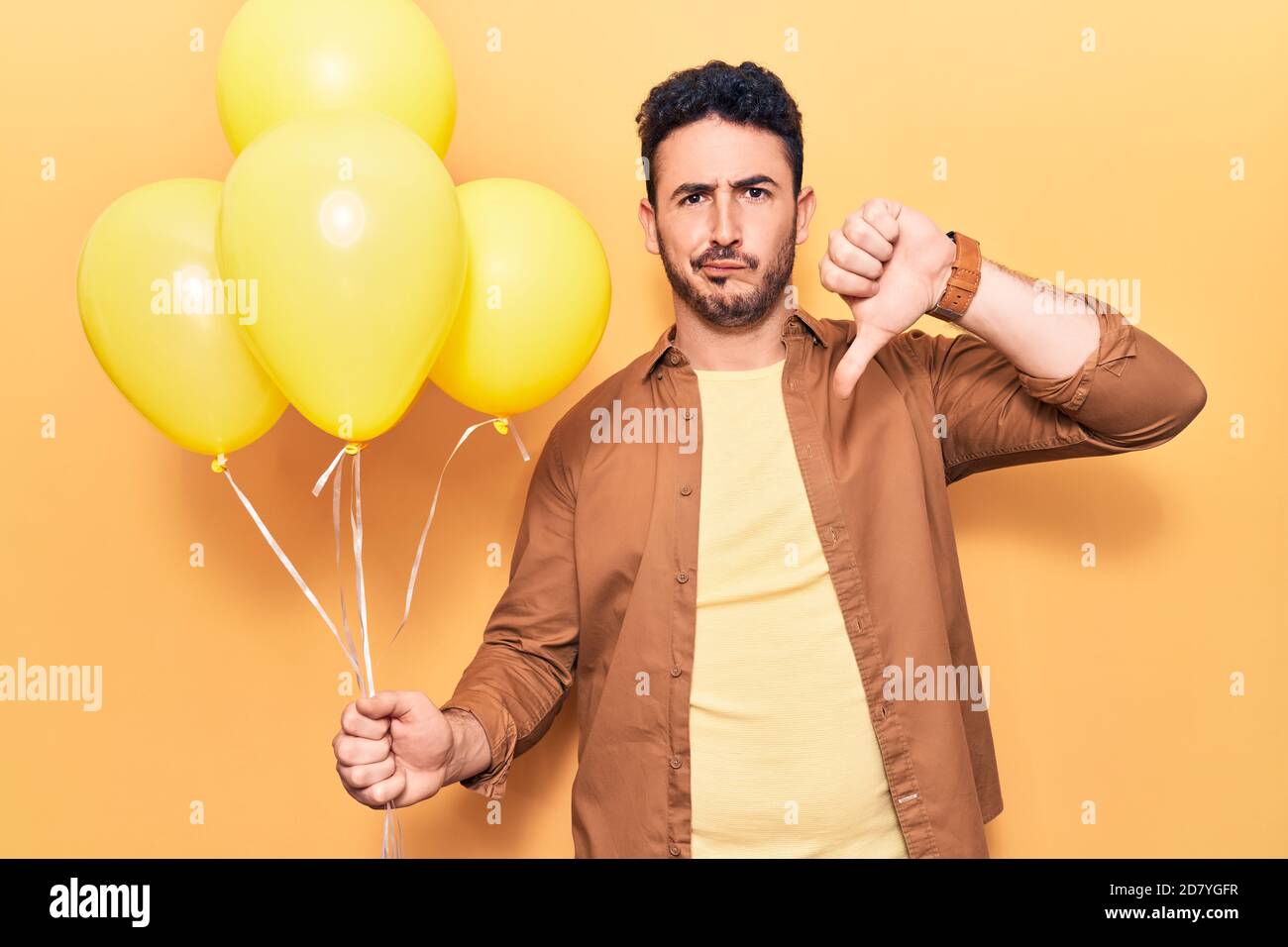 Young hispanic man holding balloons with angry face, negative sign ...