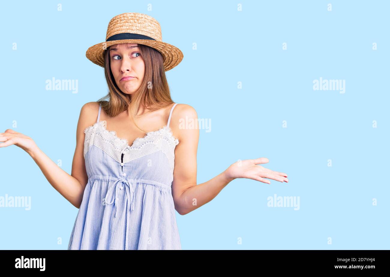Beautiful brunette young woman wearing summer hat clueless and confused ...