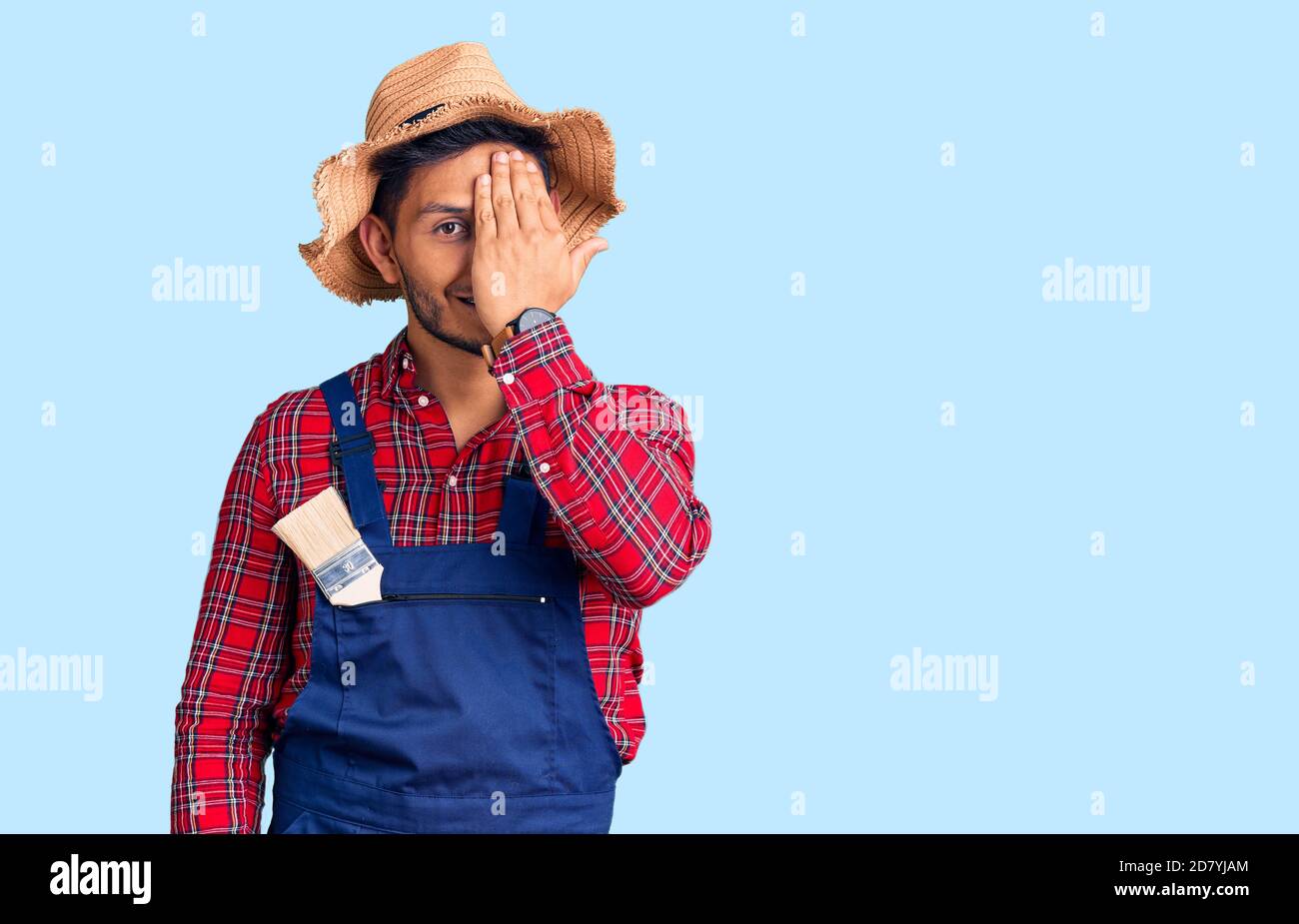 Handsome latin american young man weaing handyman uniform covering one ...