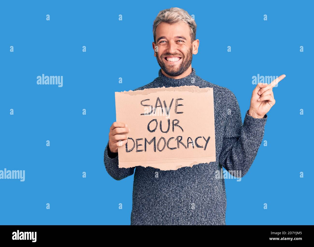 Young blond man holding save our democracy cardboard banner smiling ...