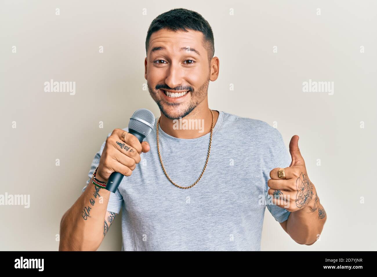 Handsome man with tattoos singing song using microphone smiling happy ...