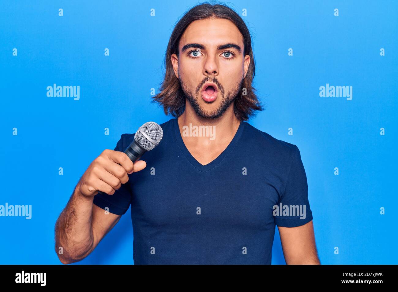 Young handsome man singing song using microphone scared and amazed with ...