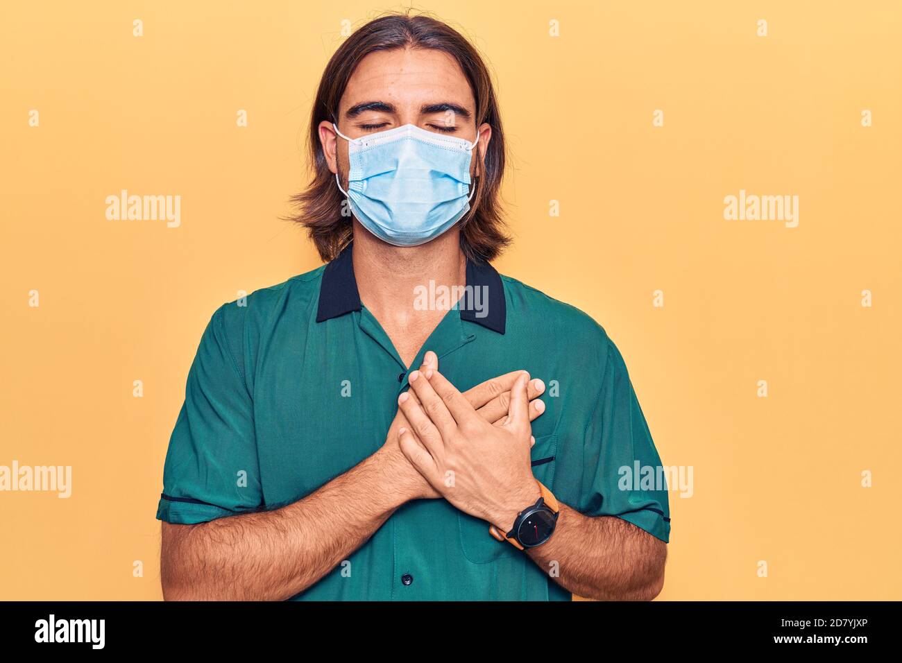 Young handsome man wearing medical mask smiling with hands on chest ...