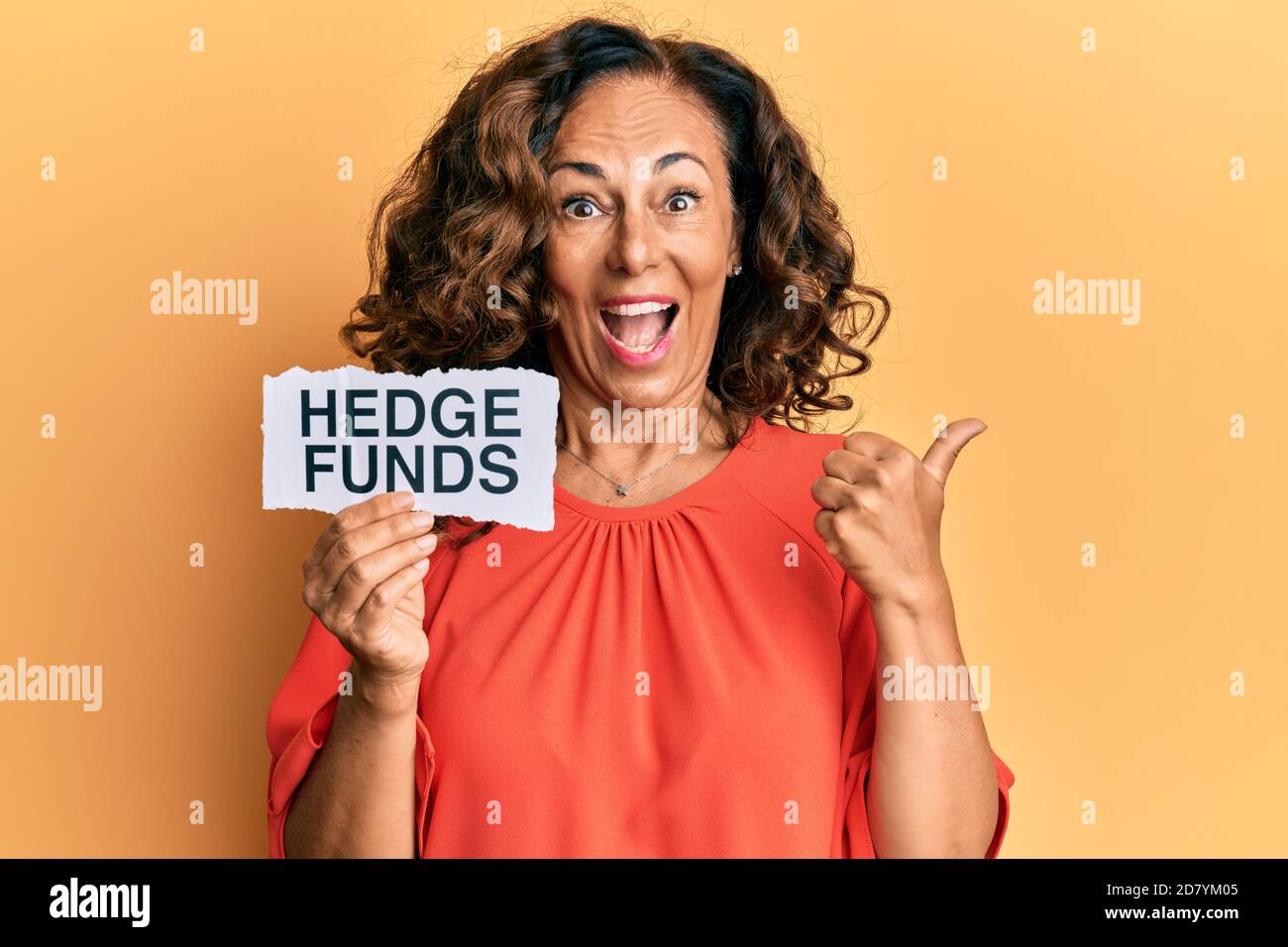Middle age hispanic woman holding hedge funds message paper pointing thumb up to the side ...