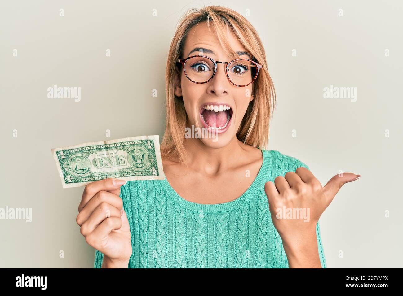 Beautiful blonde woman holding 1 dollar banknote pointing thumb up to ...