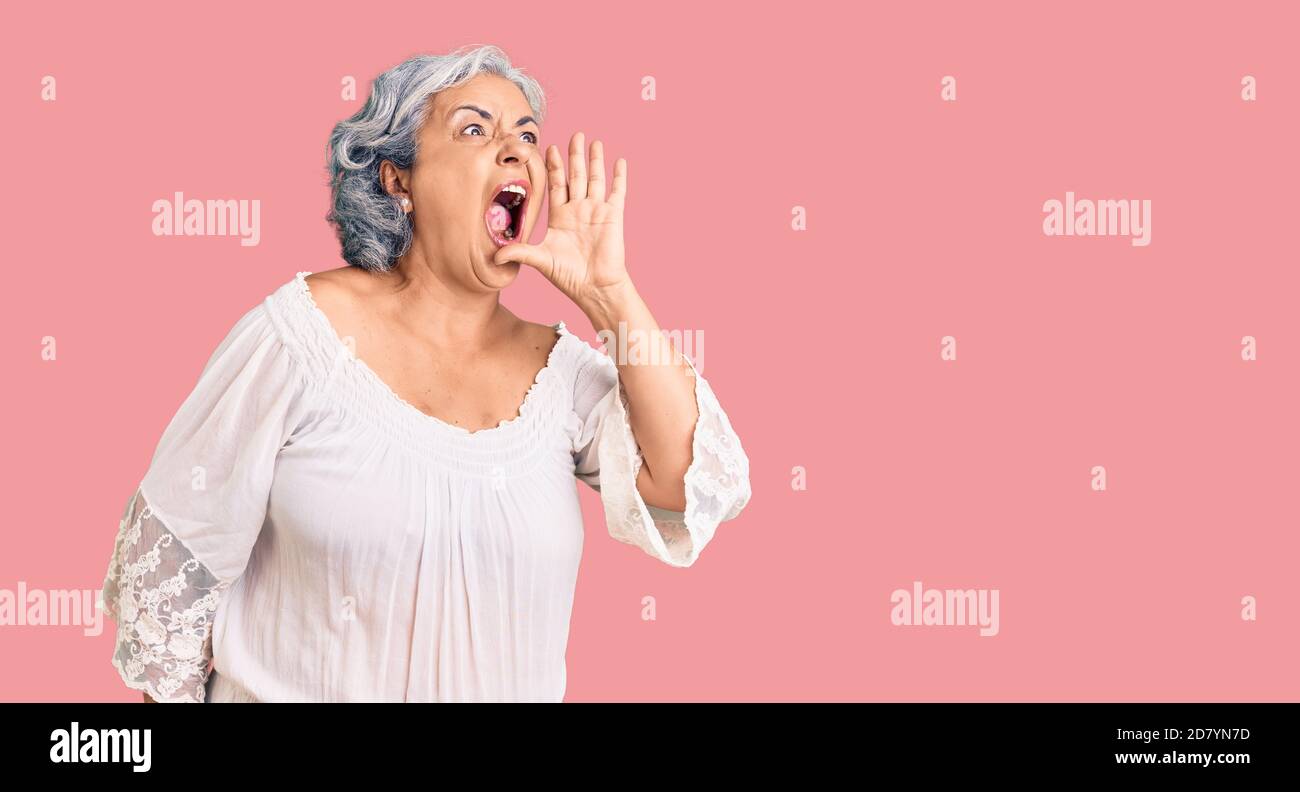 Senior woman with gray hair wearing bohemian style shouting and ...