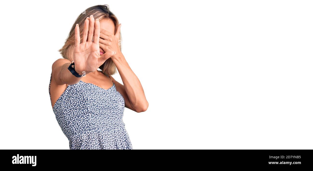 Beautiful caucasian woman wearing summer dress covering eyes with hands ...