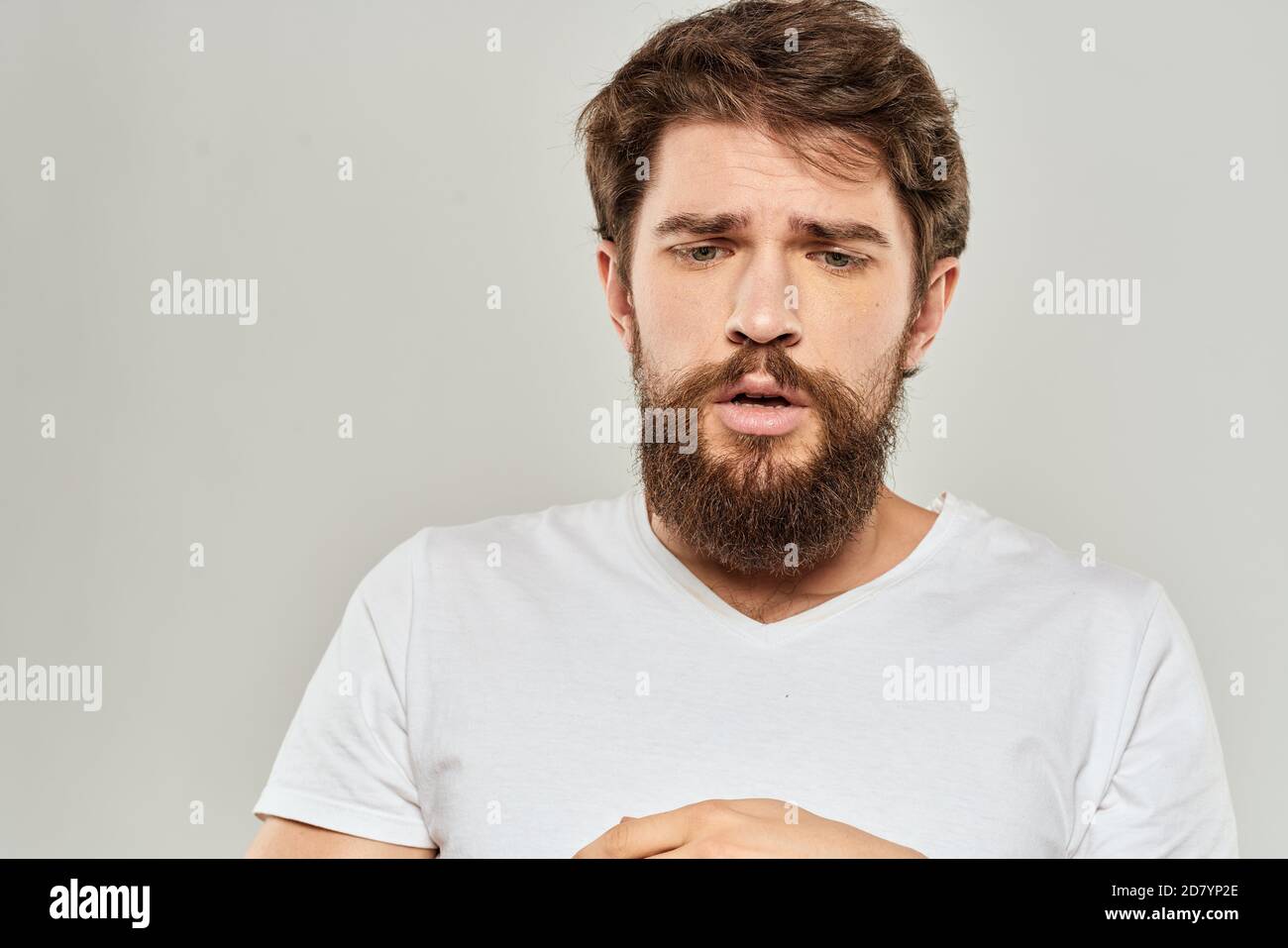 A man in a white t-shirt with a beard emotions displeased facial ...