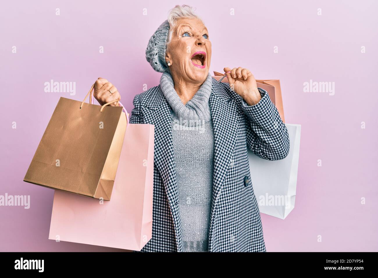 Senior grey-haired woman holding shopping bags angry and mad screaming ...