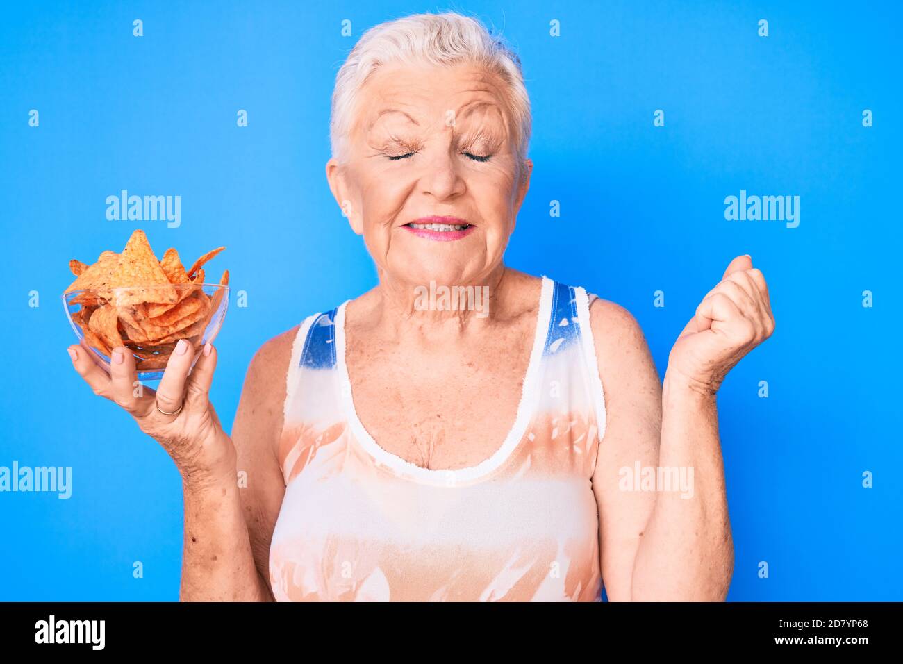 Senior beautiful woman with blue eyes and grey hair holding nachos ...
