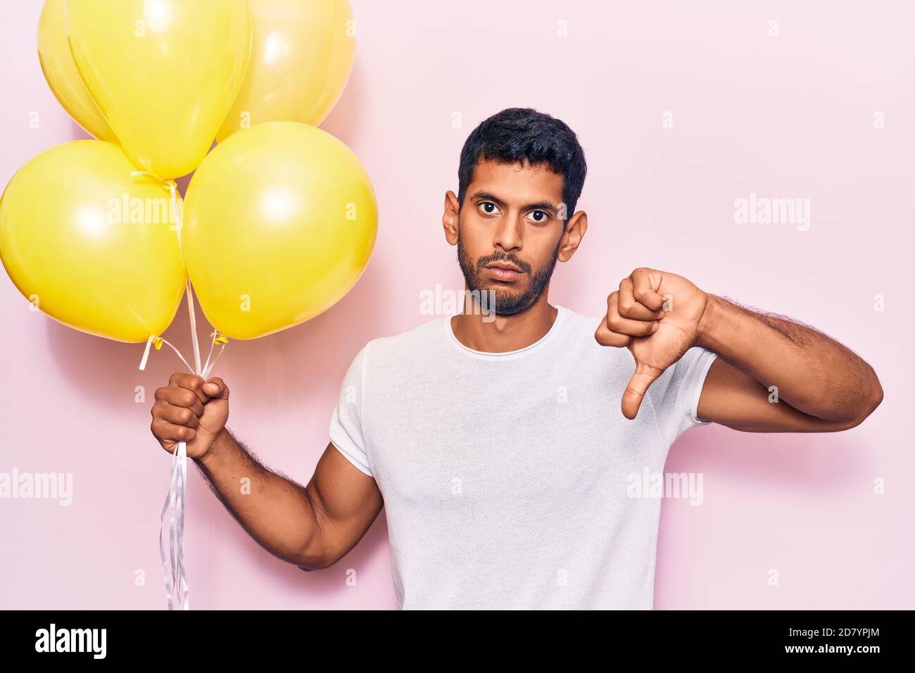 Young latin man holding balloons with angry face, negative sign showing ...