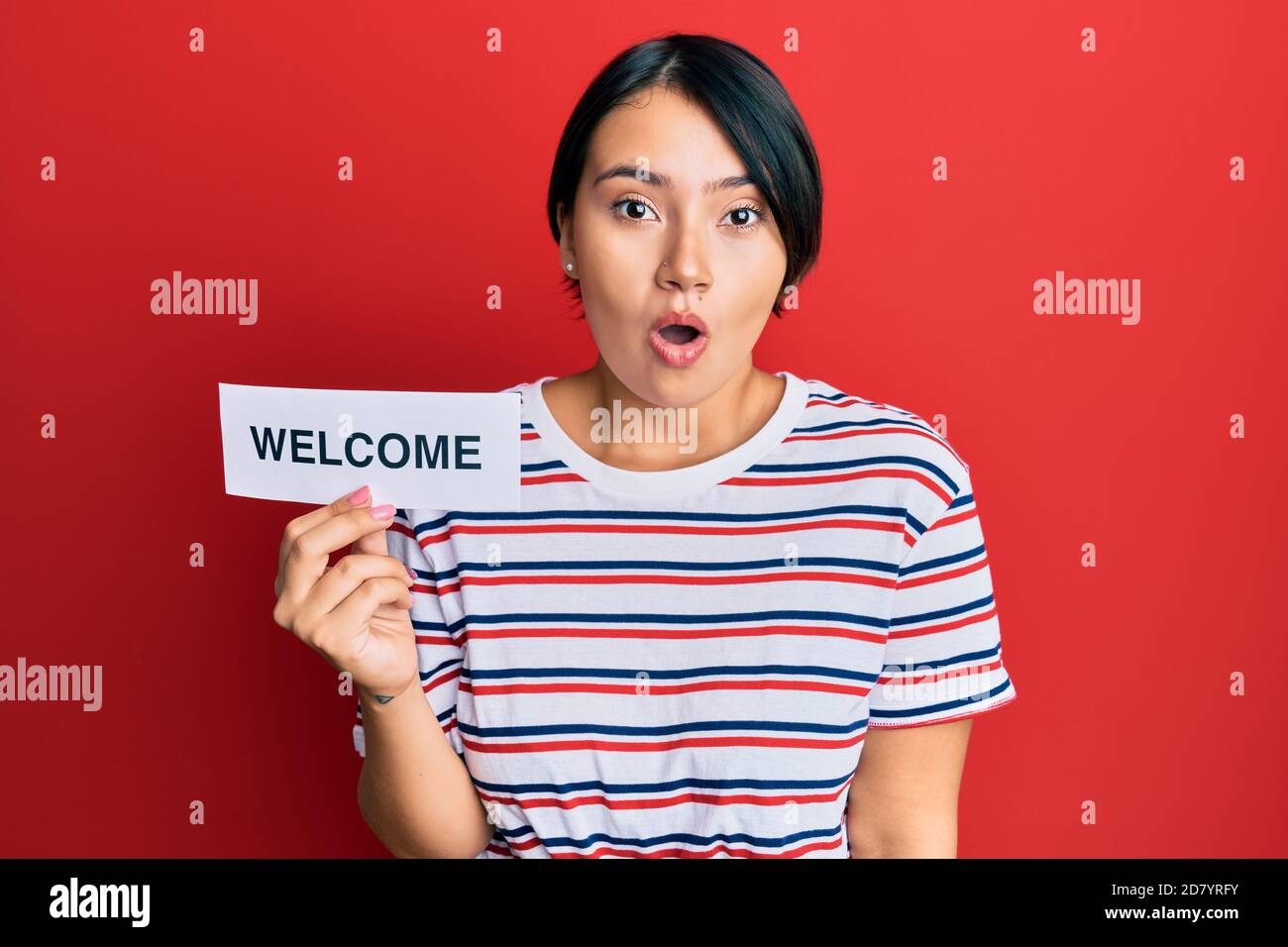 Beautiful young woman with short hair holding welcome paper scared and ...