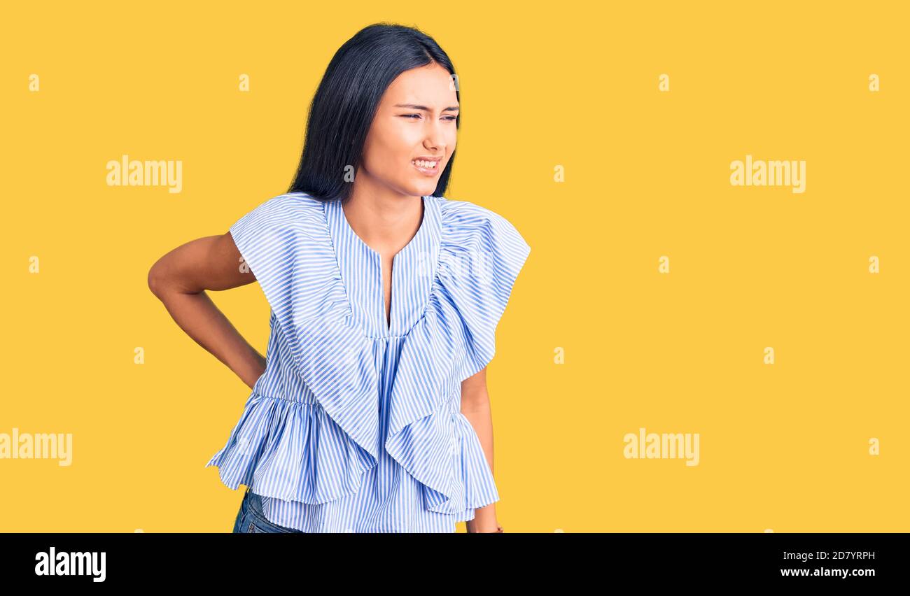 Young beautiful latin girl wearing casual clothes suffering of backache ...
