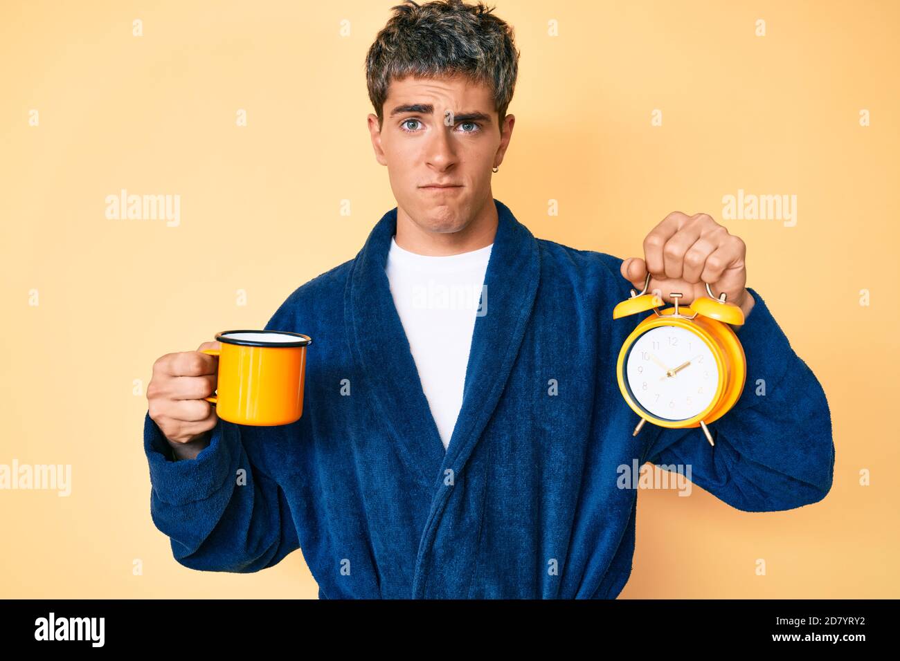 Young handsome man wearing bathrobe holding cup of coffee and alarm ...