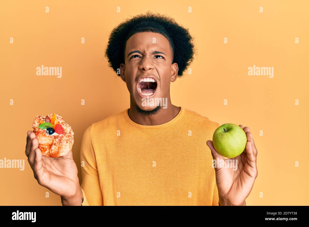 African american man with afro hair holding pastry and healthy green ...