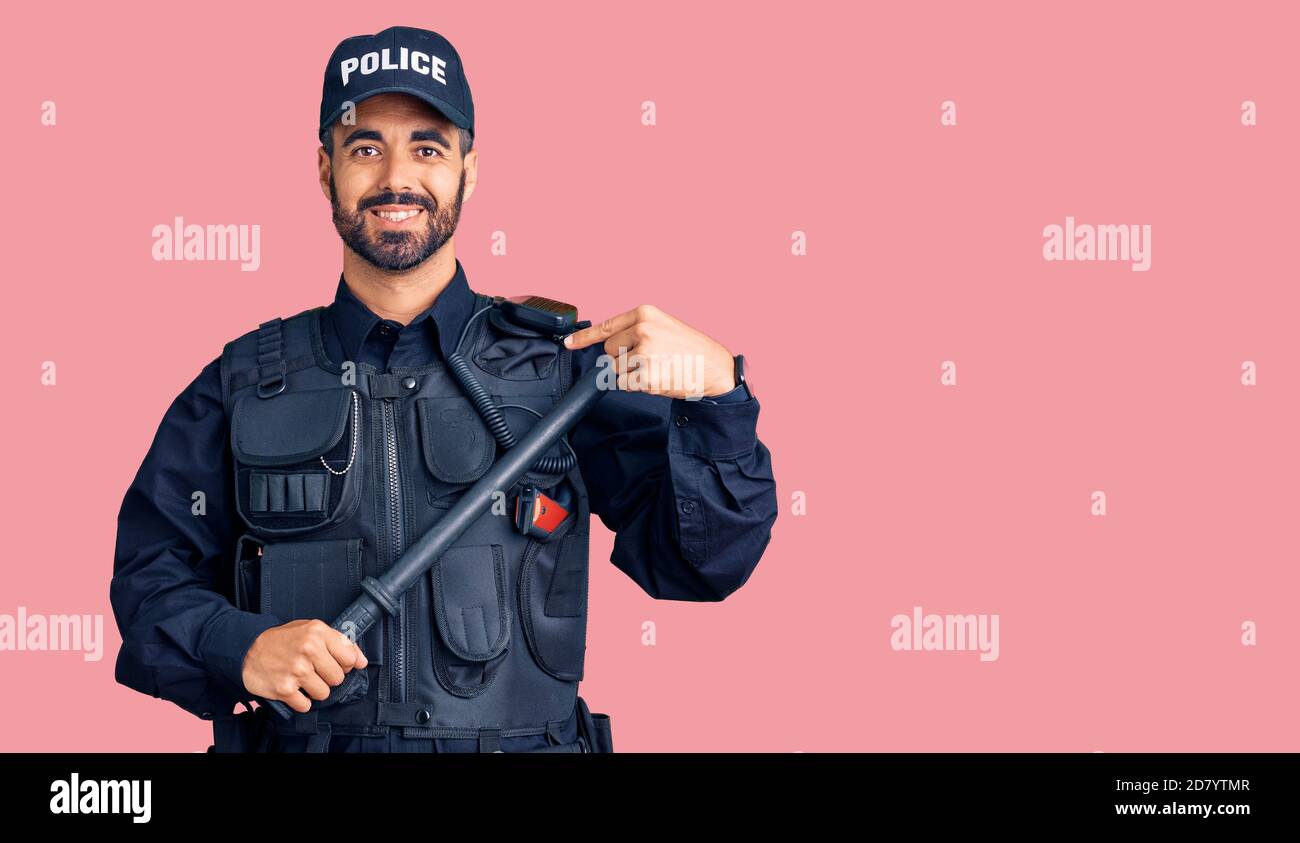 Young hispanic man wearing police uniform holding baton pointing finger ...