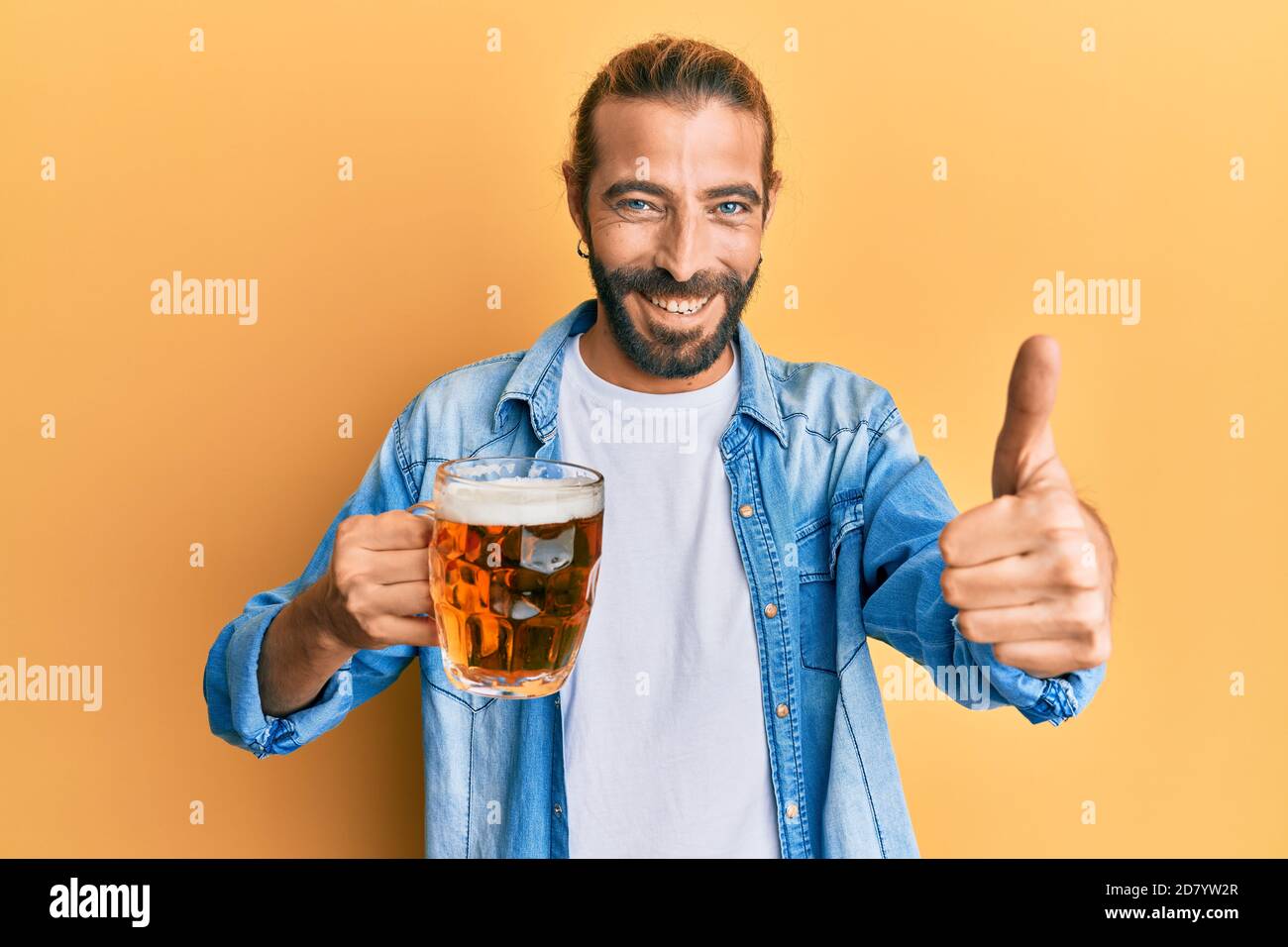 Attractive man with long hair and beard drinking a pint of beer smiling ...