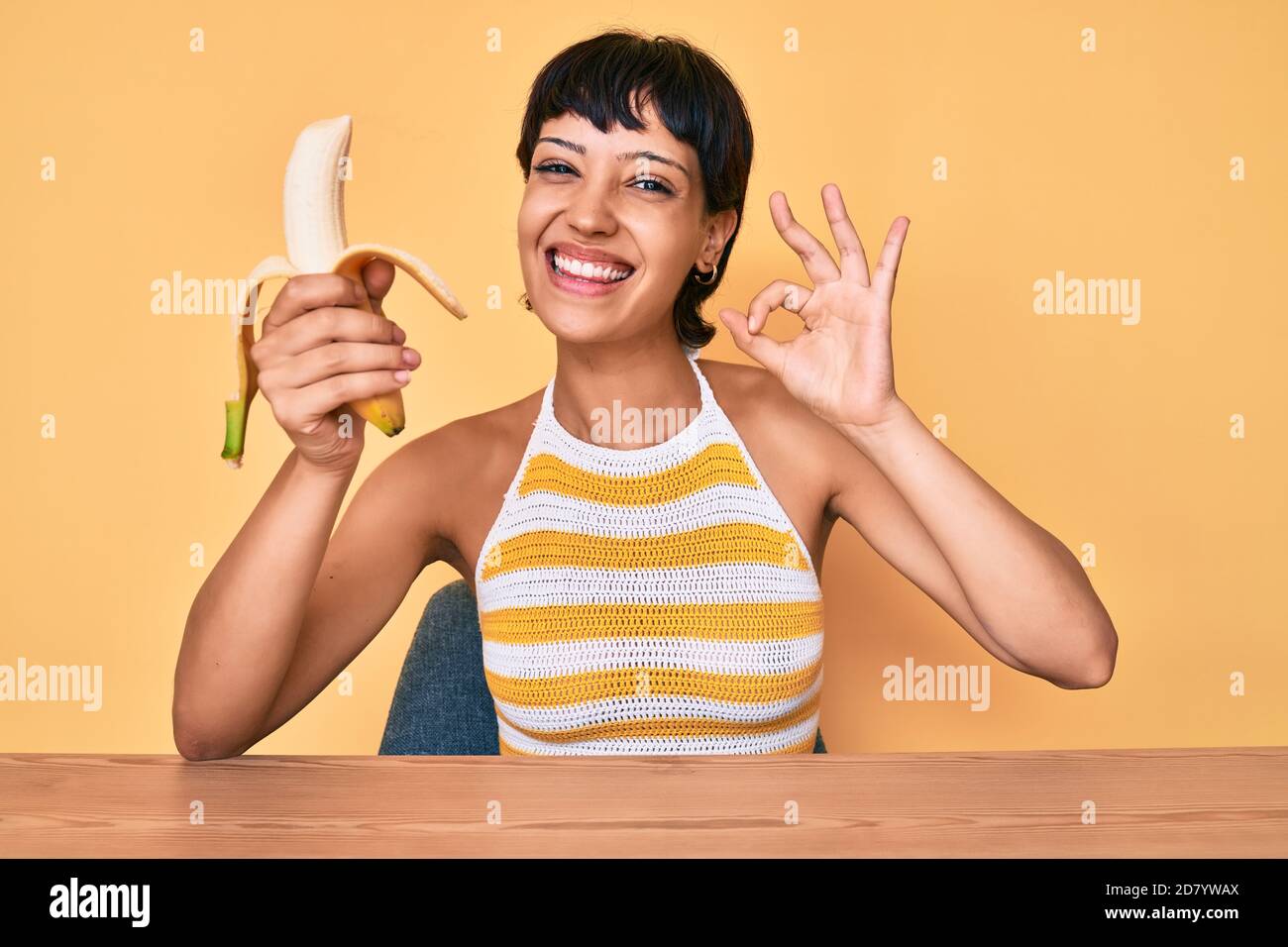 Brunette teenager girl eating banana as healthy snack doing ok sign ...